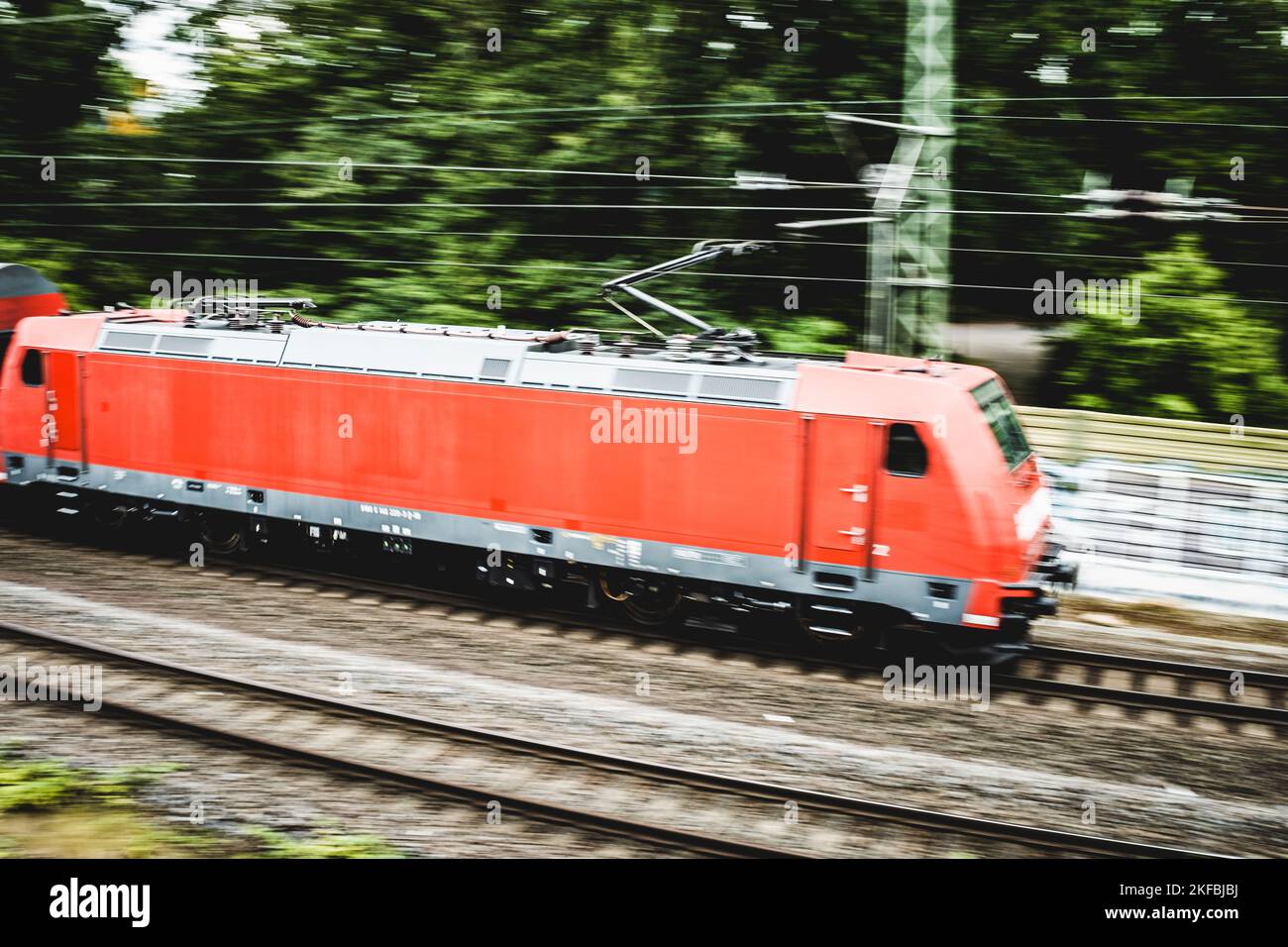 A red locomotive speeding through a green lush forest with the cables ...
