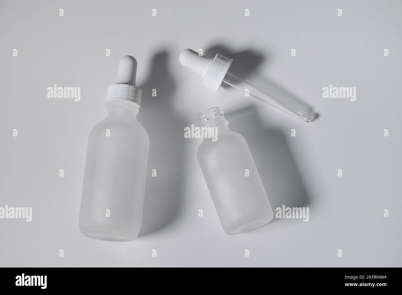 Two empty translucent glass dropper vials, one open. Flatlay of different-sized bottles on white ...