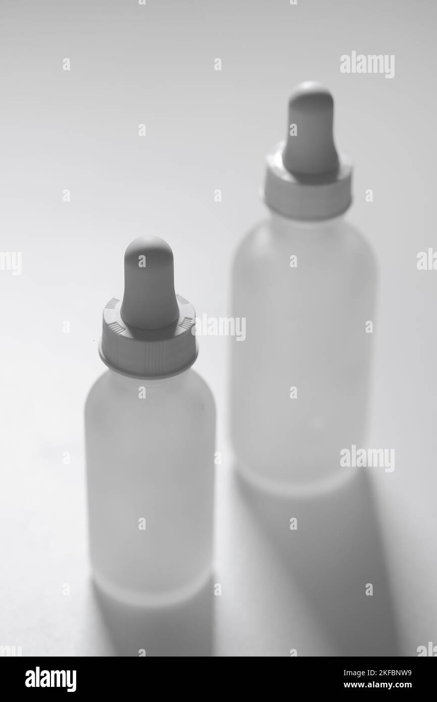 Close-up of two translucent glass dropper vials, one in focus, in front of the other. Different ...