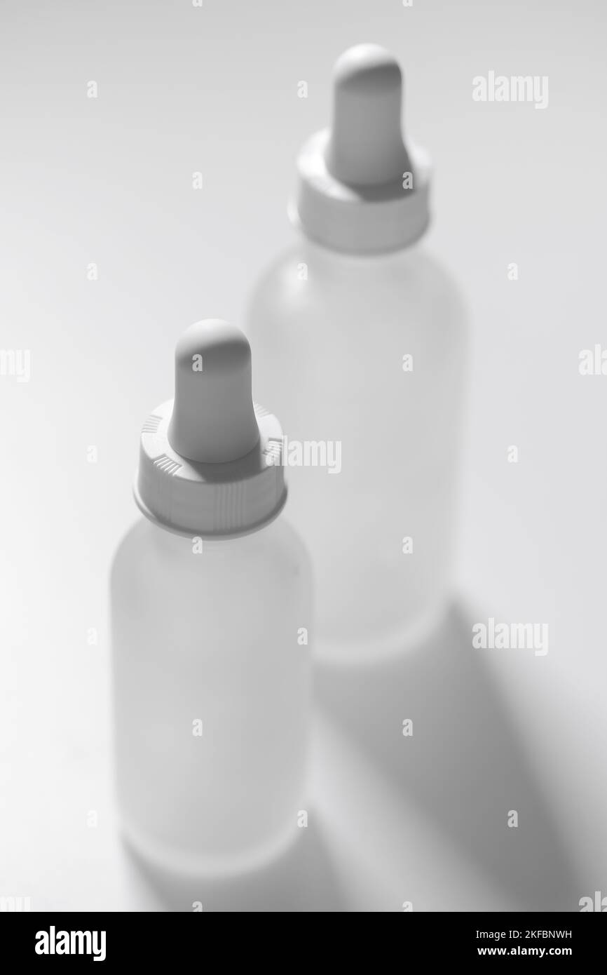 Close-up of two empty translucent glass dropper vials. Different-sized bottles on white ...