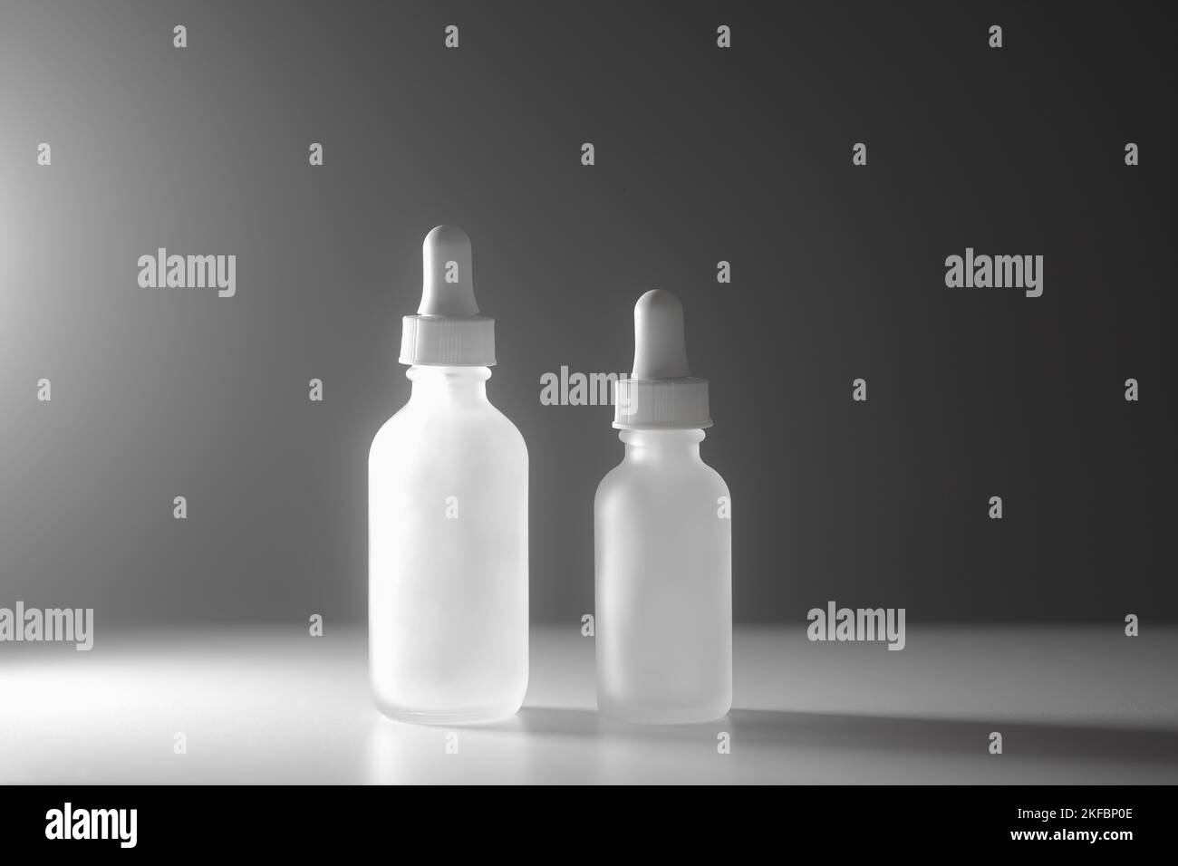 Two empty translucent glass dropper vials on two-tone white background. Different-sized bottles ...