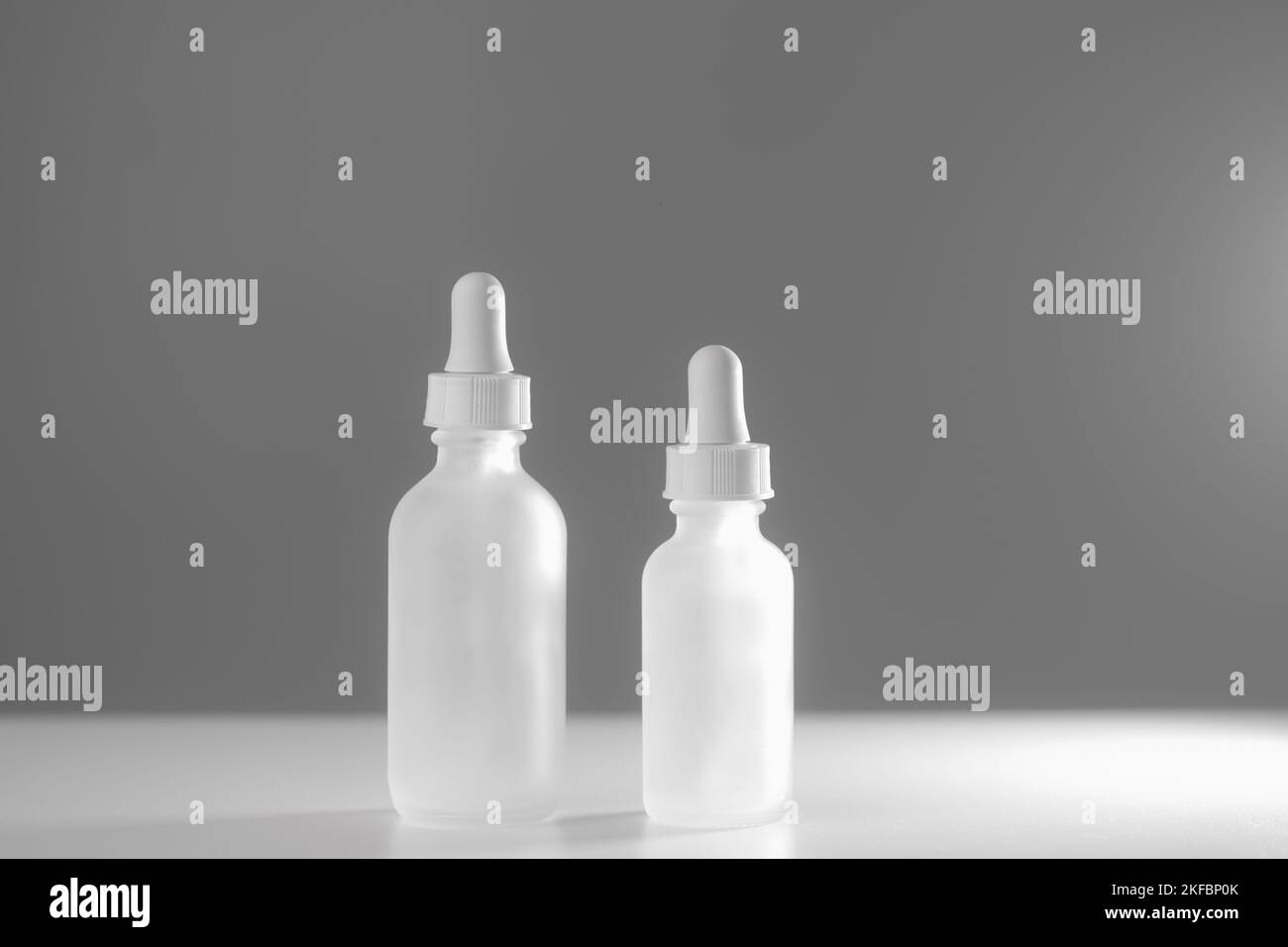 Two empty translucent glass dropper vials on two-tone white background. Different-sized bottles ...