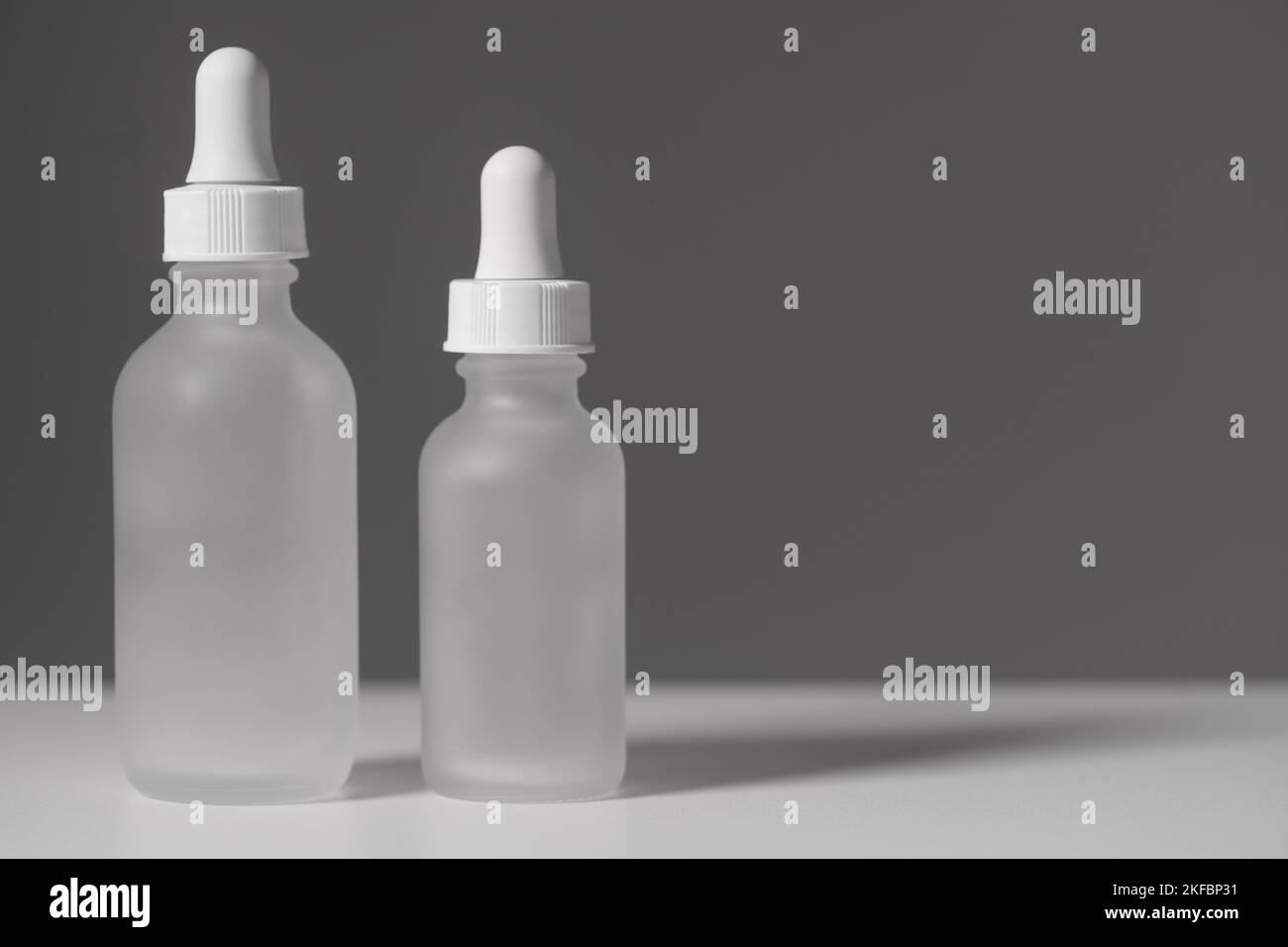 Close-up of two empty translucent glass dropper vials. Different-sized bottles on two-tone white ...