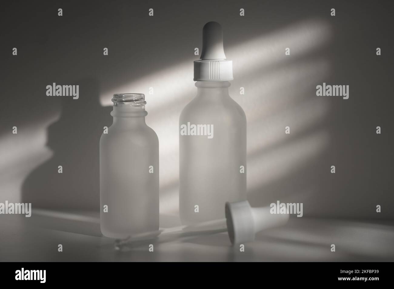 Two empty translucent glass dropper vials, one open. Different-sized bottles on white background ...