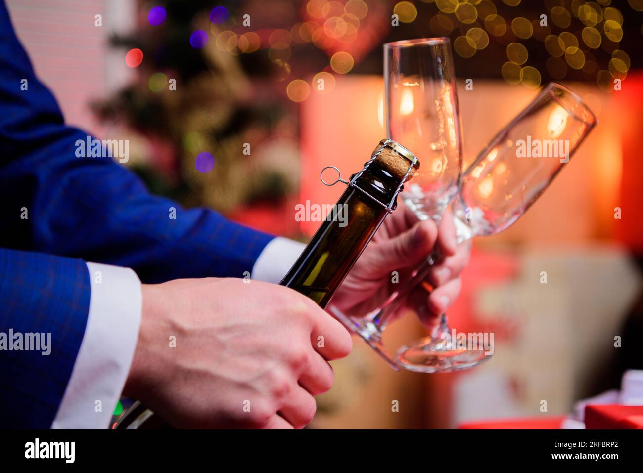Male hands opening champagne bottle on christmas decorations background. Open champagne and ...