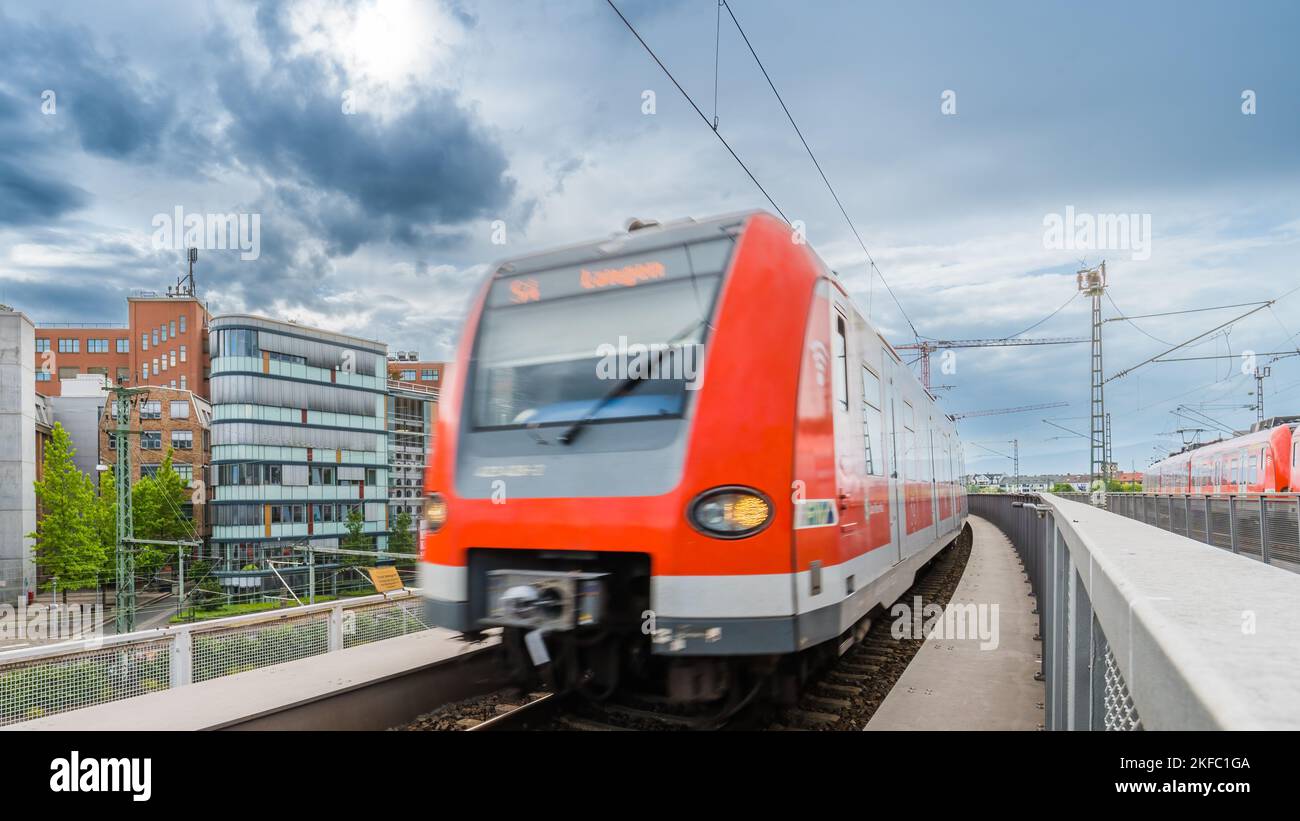 A local, moving train under the cloudy sky, surrounded by buildings ...