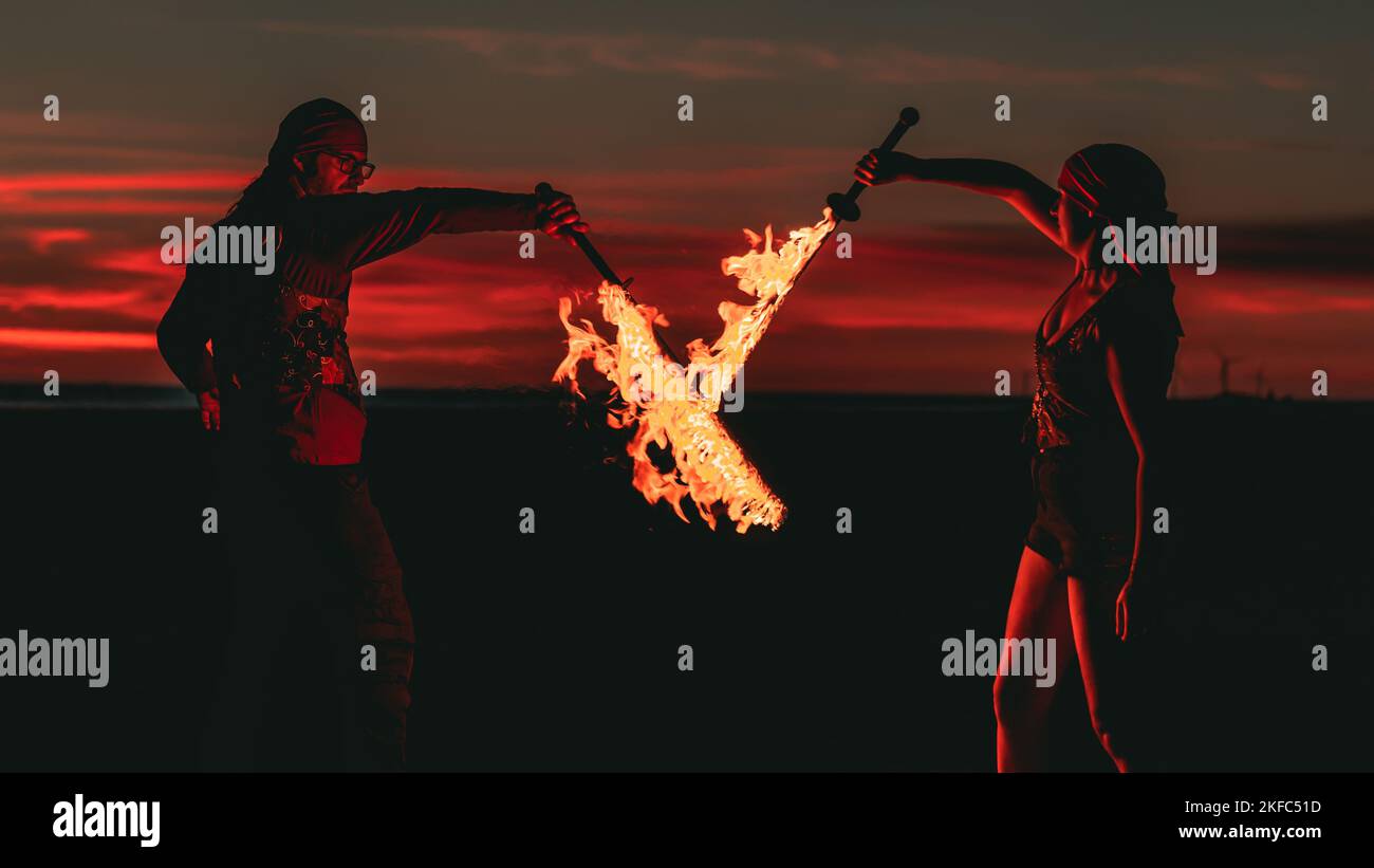 A panoramic of two people fighting with fire swords on a beach during a ...