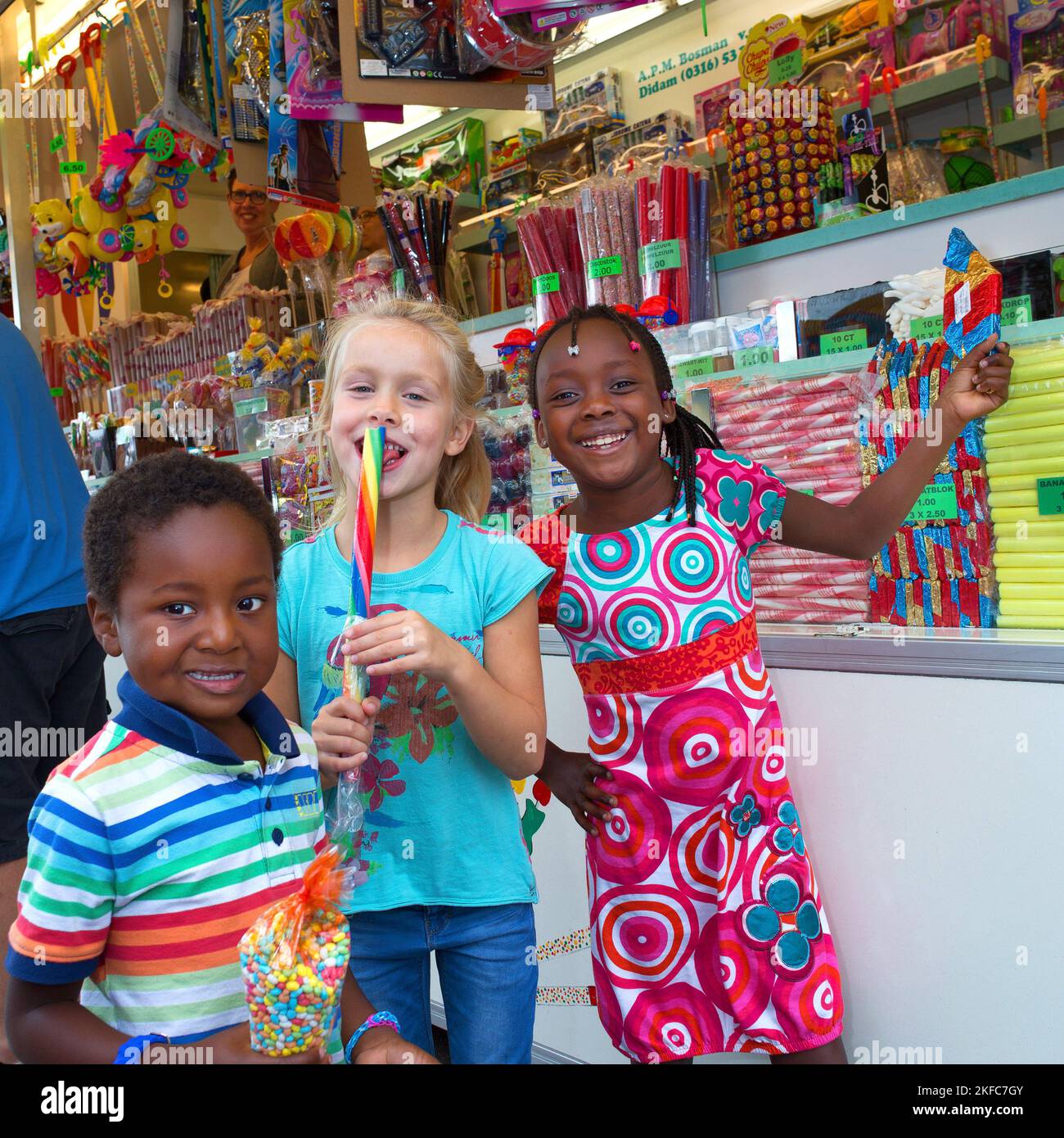 three little children at a candy stal with a candy cane at a fair ...