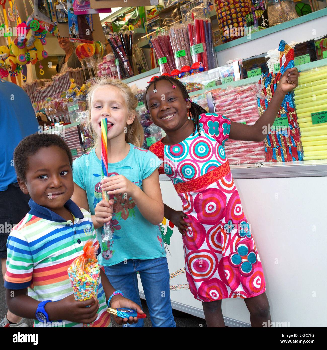 three little children at a candy stal with a candy cane at a fair ...