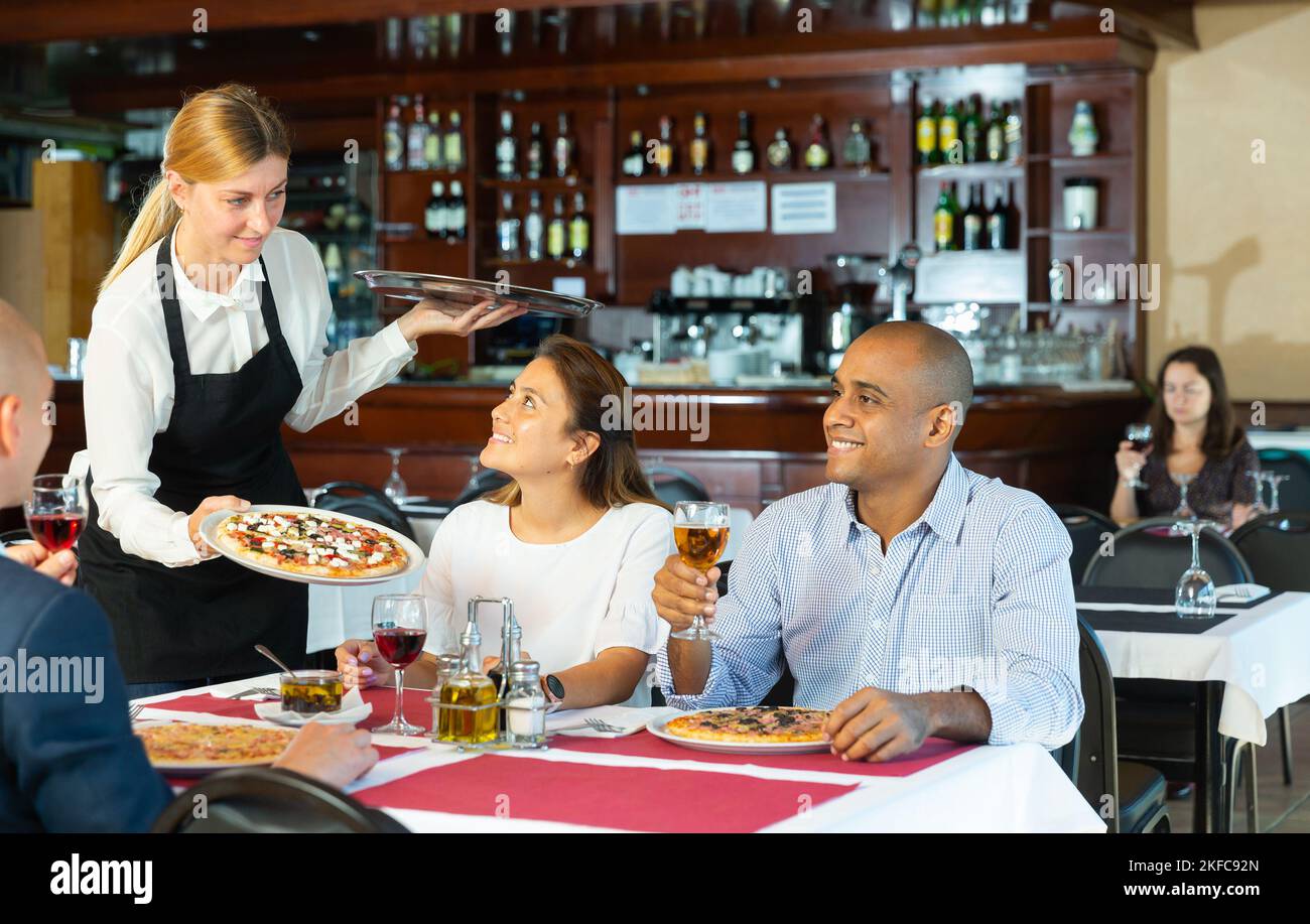 Polite female waiter bringing ordered pizza to friends Stock Photo - Alamy