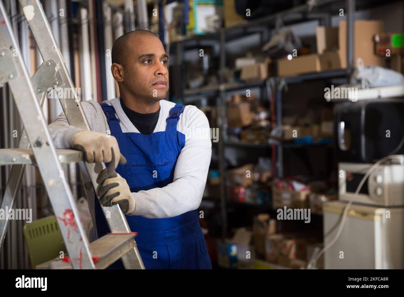 Positive warehouse worker stands next to stepladder and tool shelves in hardware store Stock ...