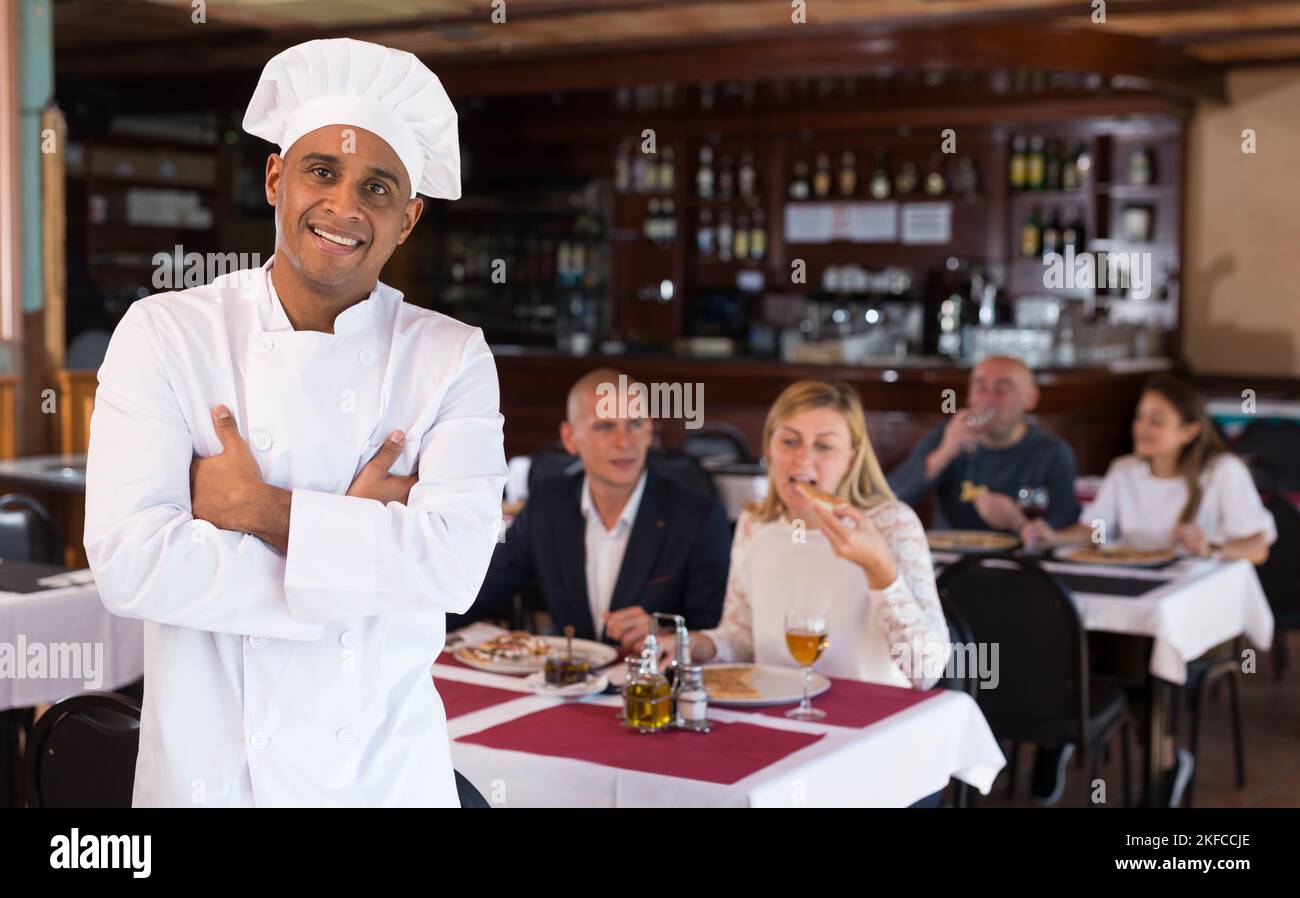 Portrait of positive chef against the background of dining guests in ...