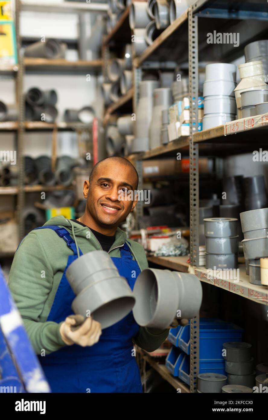 Worker in overalls lays out plumbing fittings on the shelves of ...