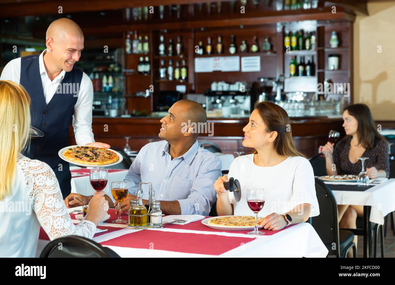 Smiling waiter serving pizza to group of people in restaurant Stock ...