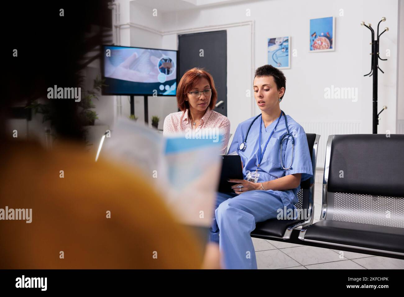 Medical assistant consulting asian woman in hospital lobby, taking ...