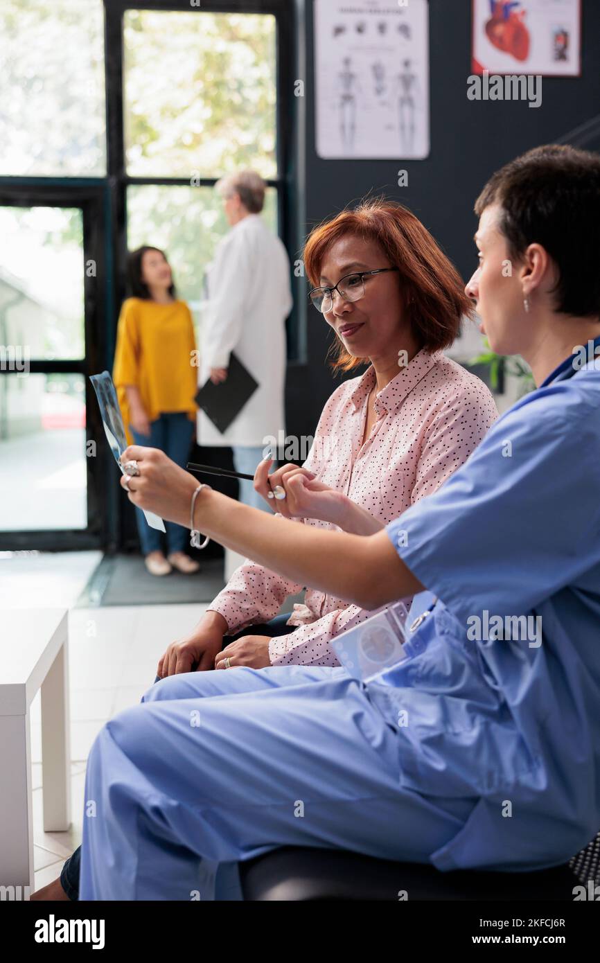Medical assistant explaining bones x ray diagnosis to senior patient sitting in waiting area at ...