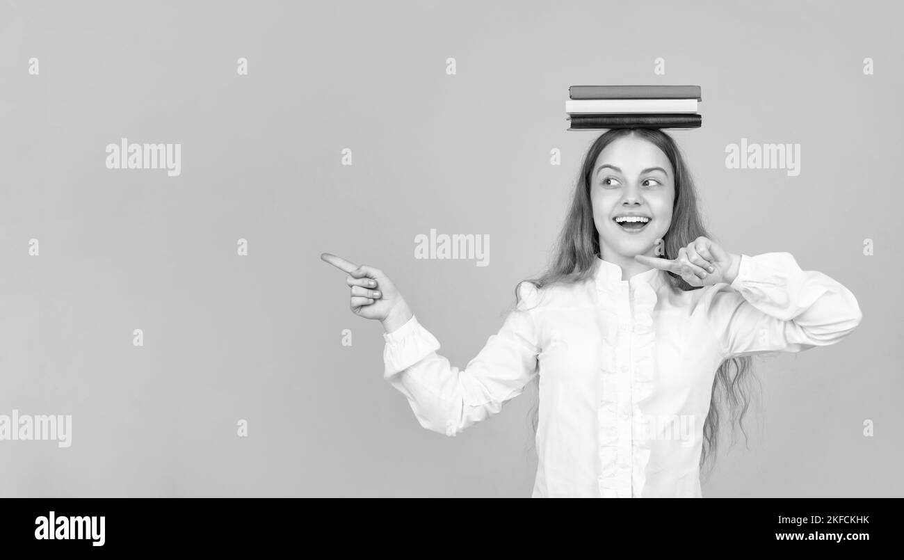 happy kid in white shirt with book stack on head pointing finger on ...
