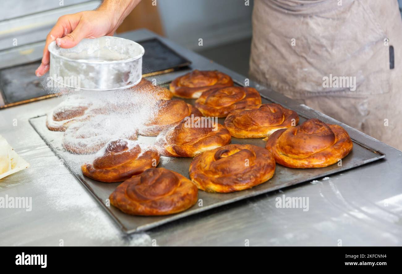 Baker sprinkles icing sugar on buns at bakery Stock Photo - Alamy
