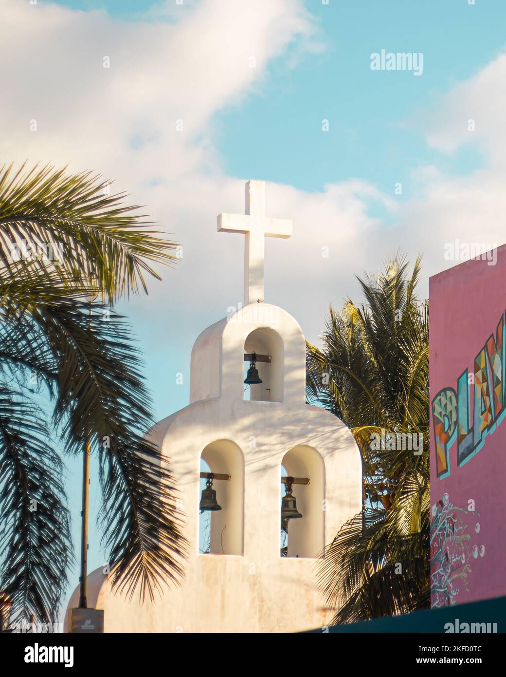 A vertical closeup shot of a white church spire with a cross near palm ...