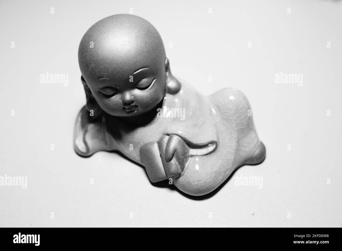 A grayscale shot of a resting monk sculpture with a book in his hand ...