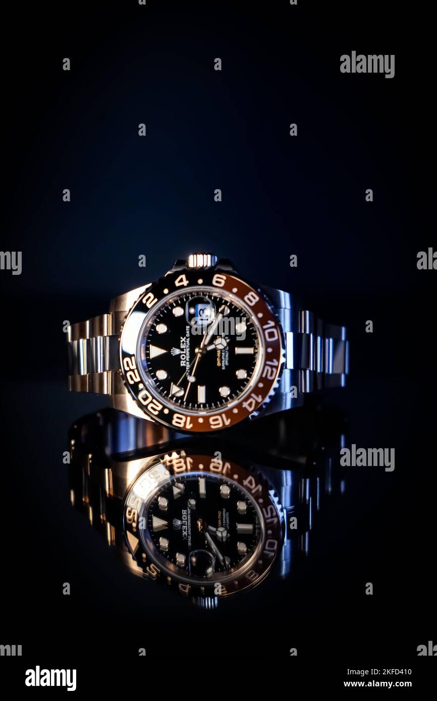 A vertical shot of rosegold Rolex on reflective surface on black ...