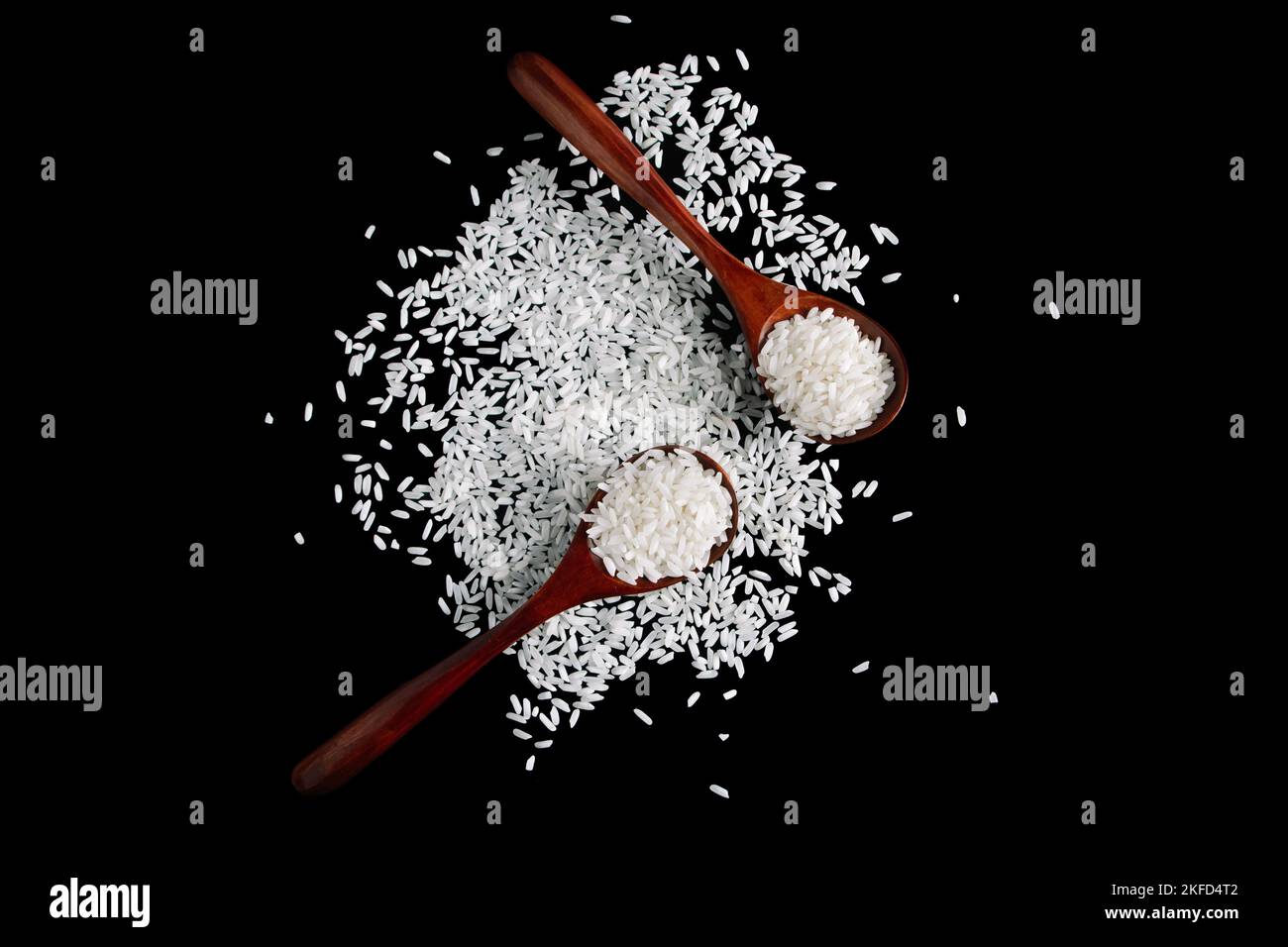 White uncooked rice in wooden spoons on black background. Raw grains of ...