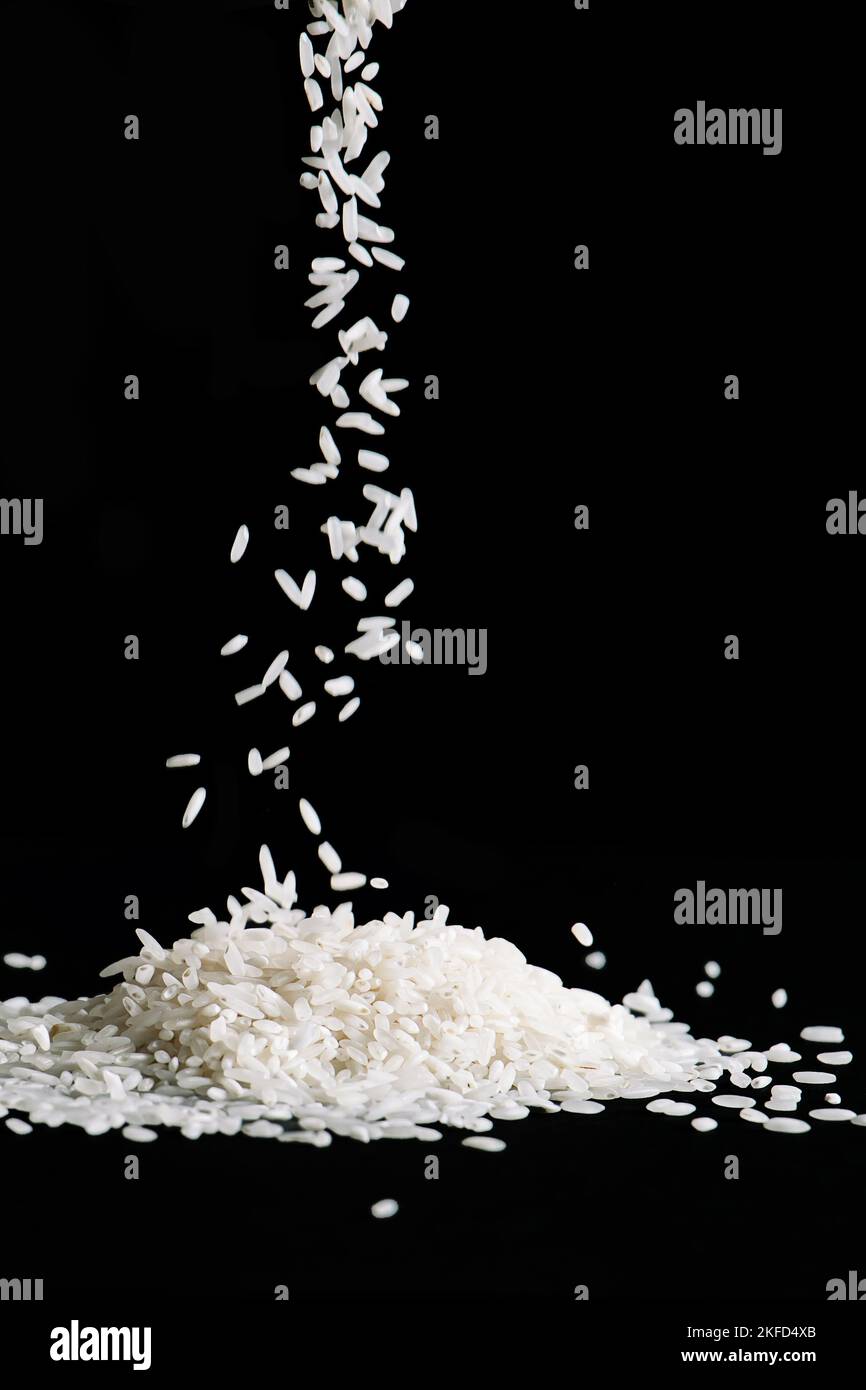 Raw white rice is falling on table. Pile of uncooked long rice on black ...