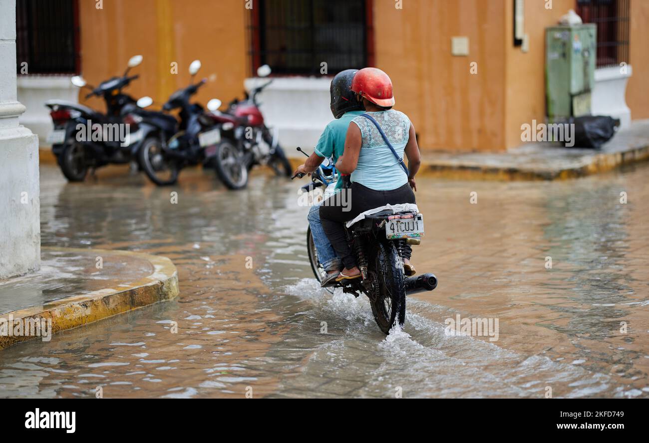 A motorcycle driving through deep water on the road after hurricane in ...