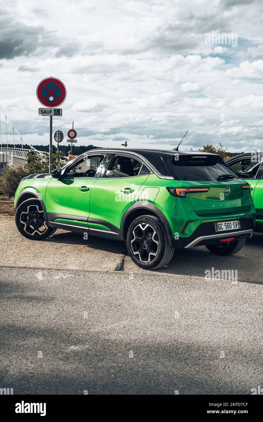 A vertical shot of a modern green Opel Mokka 2022 car against a cloudy ...
