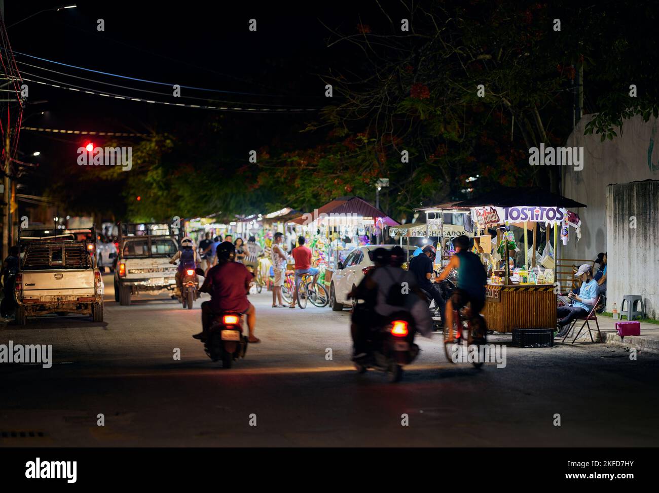 A night view of bikes and cars in the street and food booth during ...