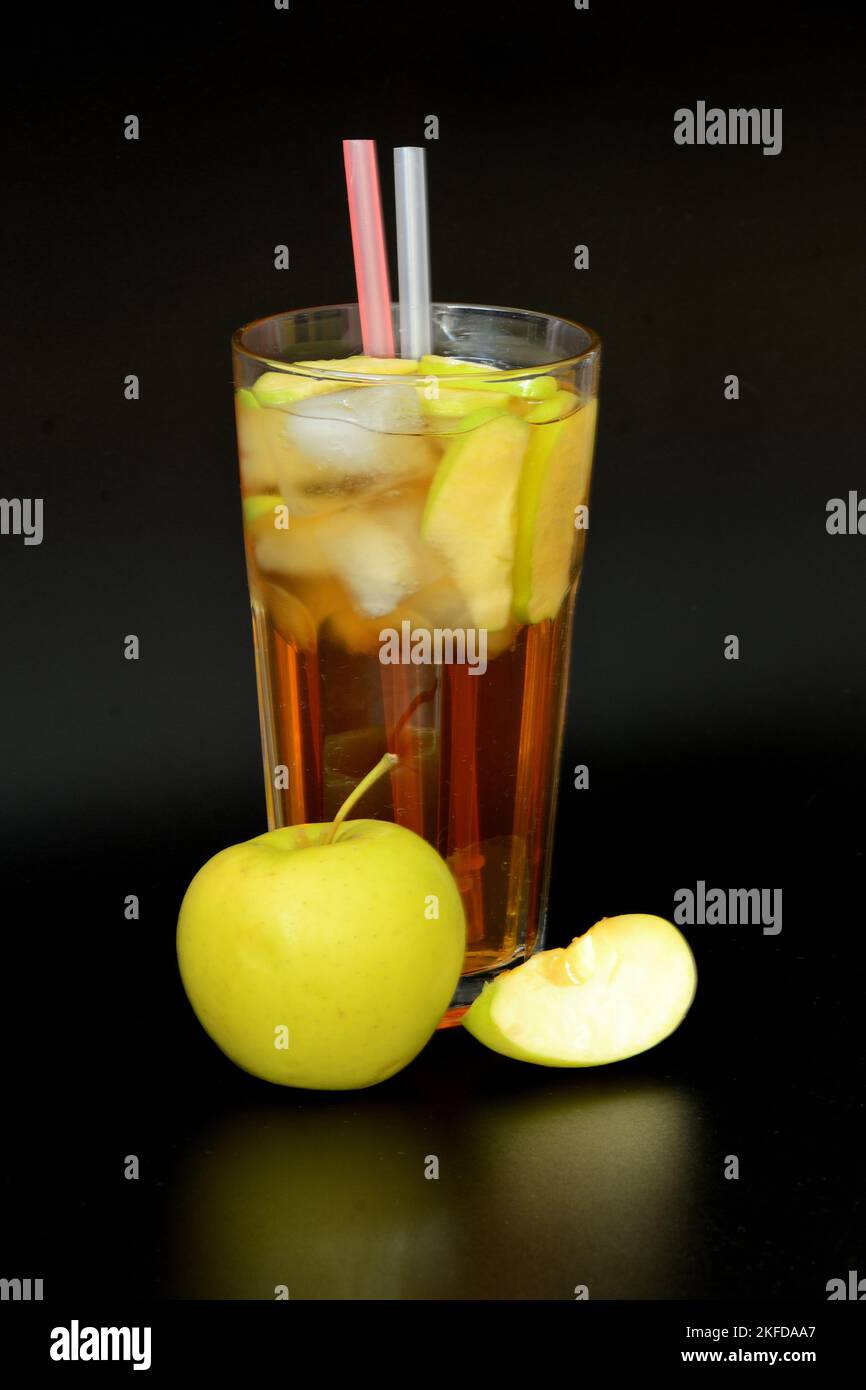 A tall glass of fruit juice with ice and straws on a black background ...