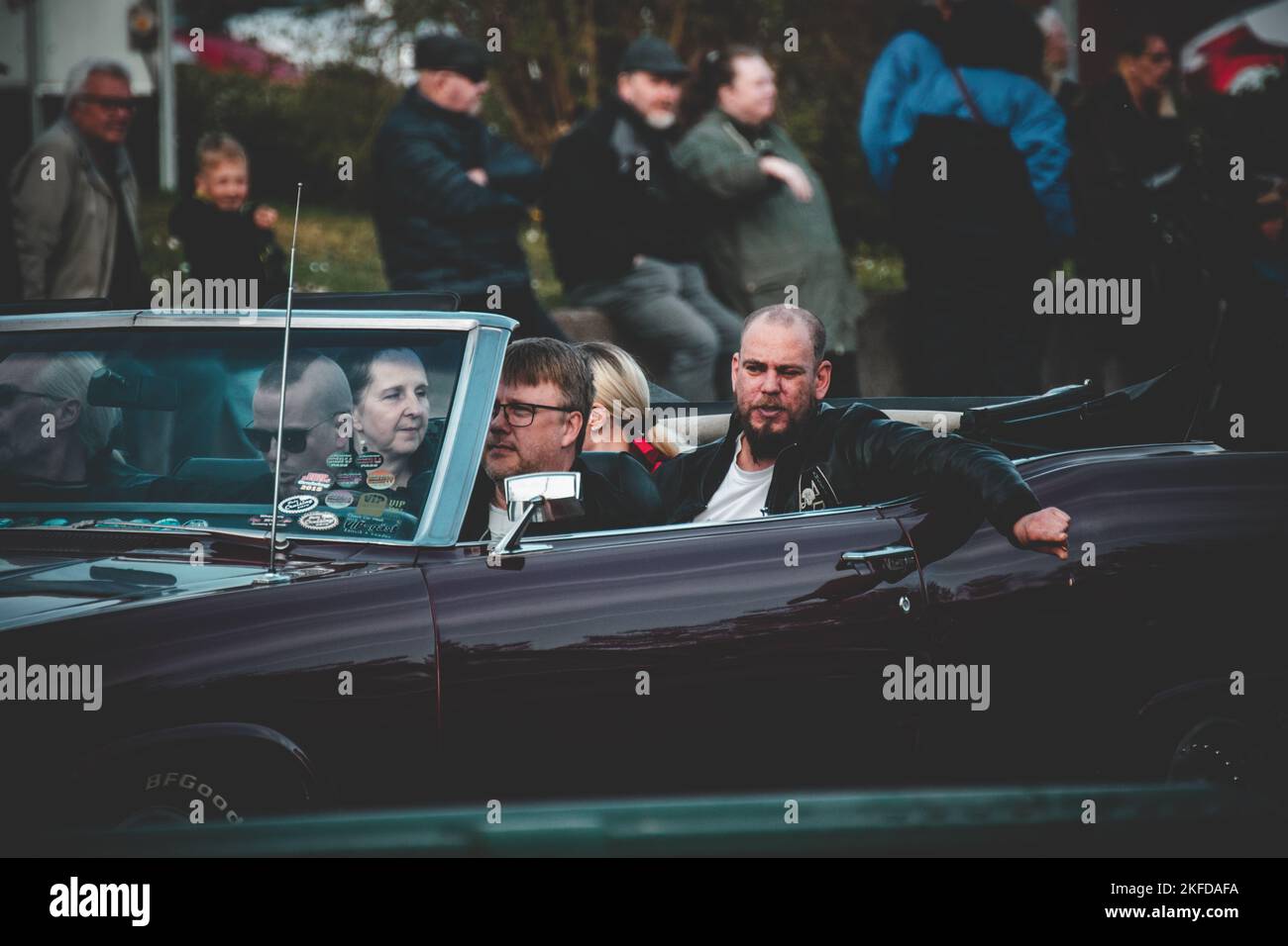 A group of young people riding an old black car during the Reggae event ...