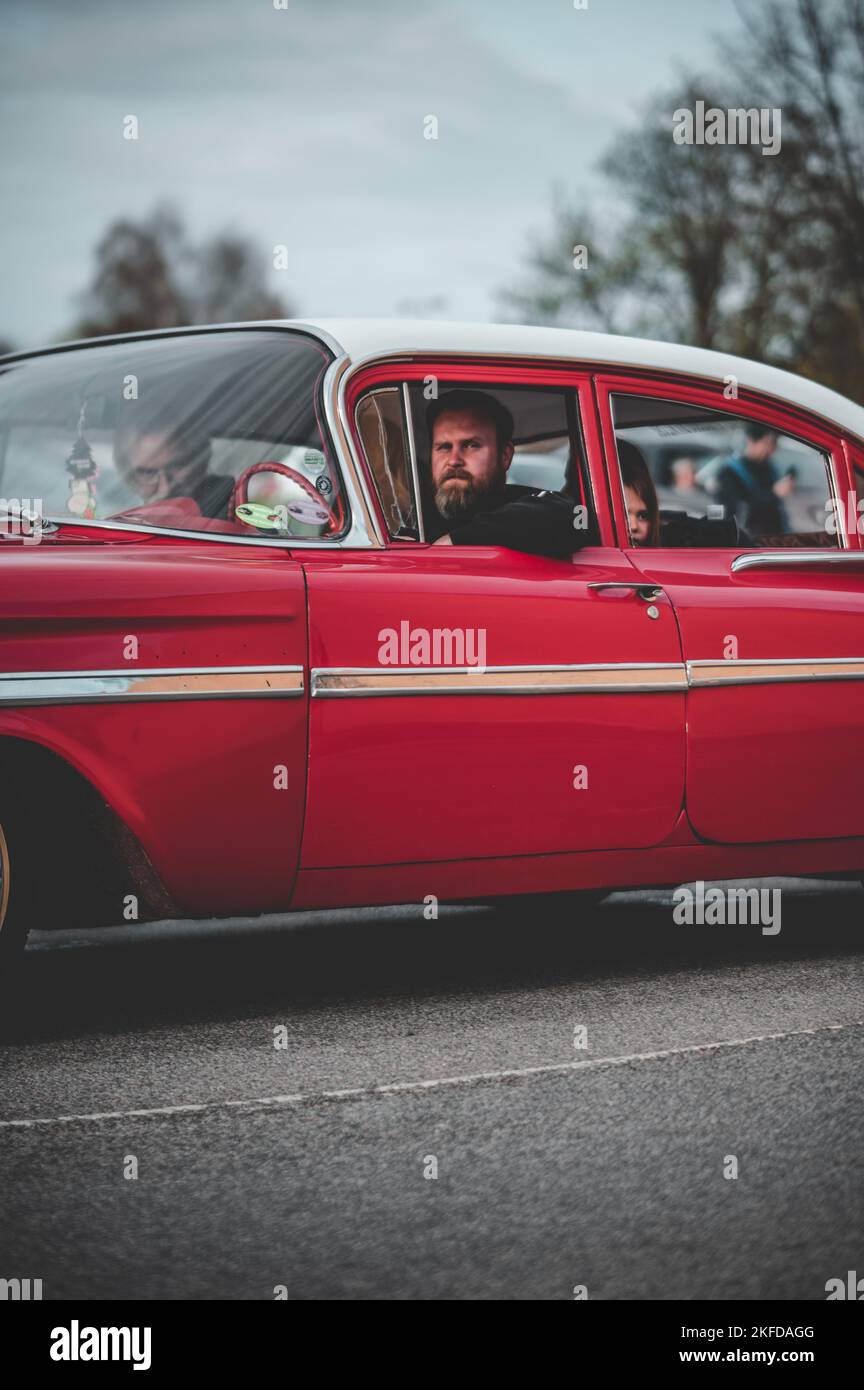 A vertical of a bearded man driving a retro car at a cruising event ...