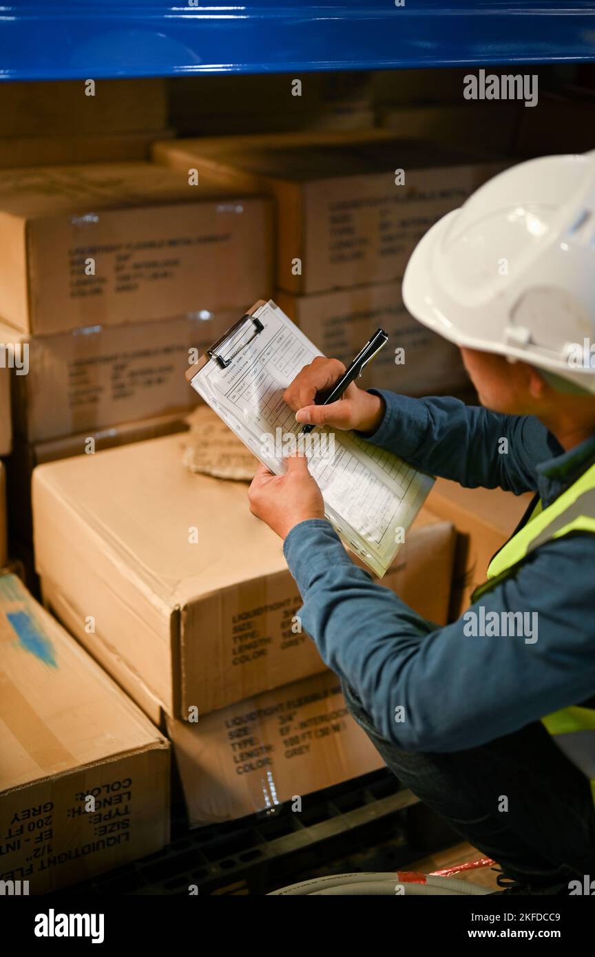 Concentrated Asian male warehouse worker in white hardhat and uniform ...