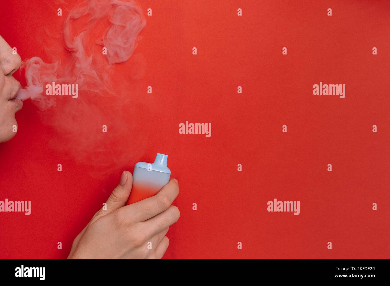 Inhalation of smoke from vape in female hand against red background ...