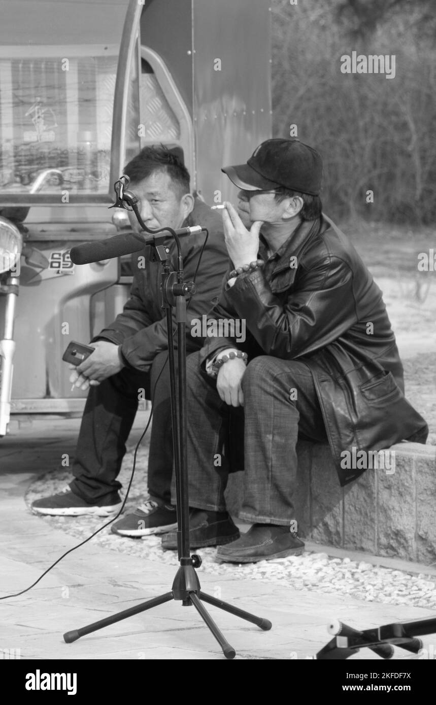 A vertical of two men one of whose is smoking sitting in the street ...