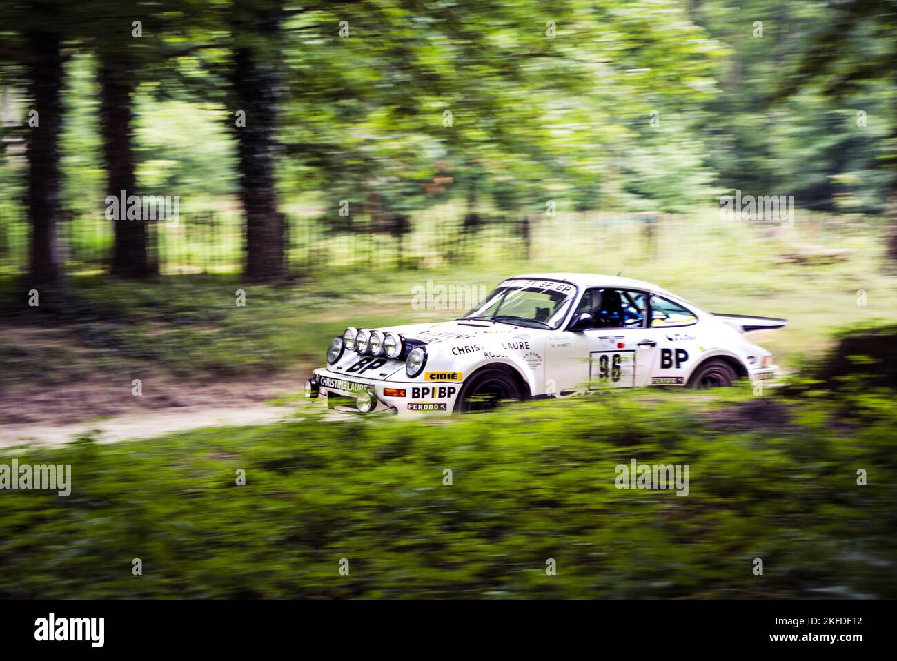 A white rally car racing on the road through a green forest at the ...
