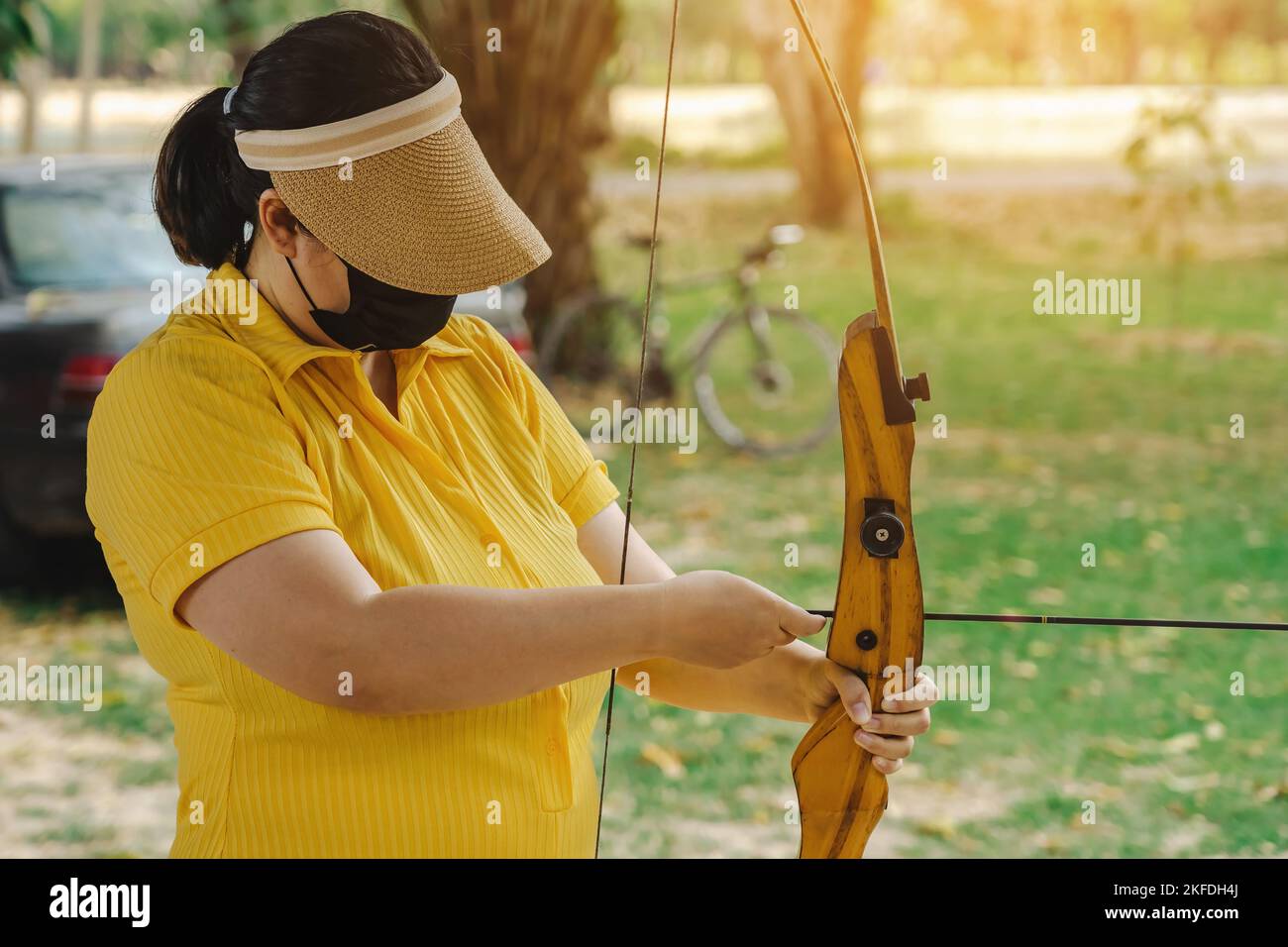 Asian woman wear visor with face mask aims archery bow and arrow to ...