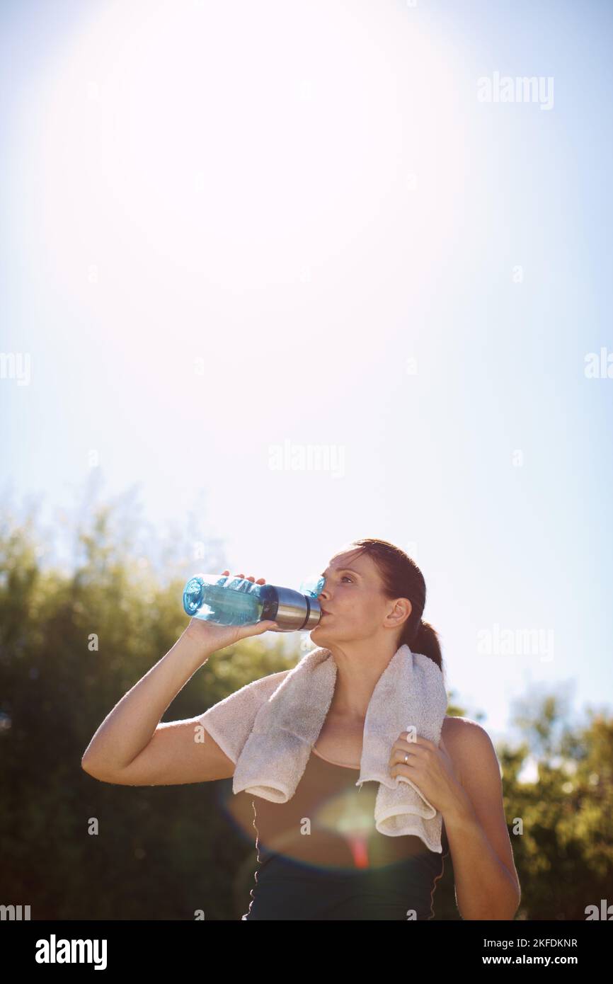 Hydrating after a good workout. An attractive woman drinking from her water bottle after a ...