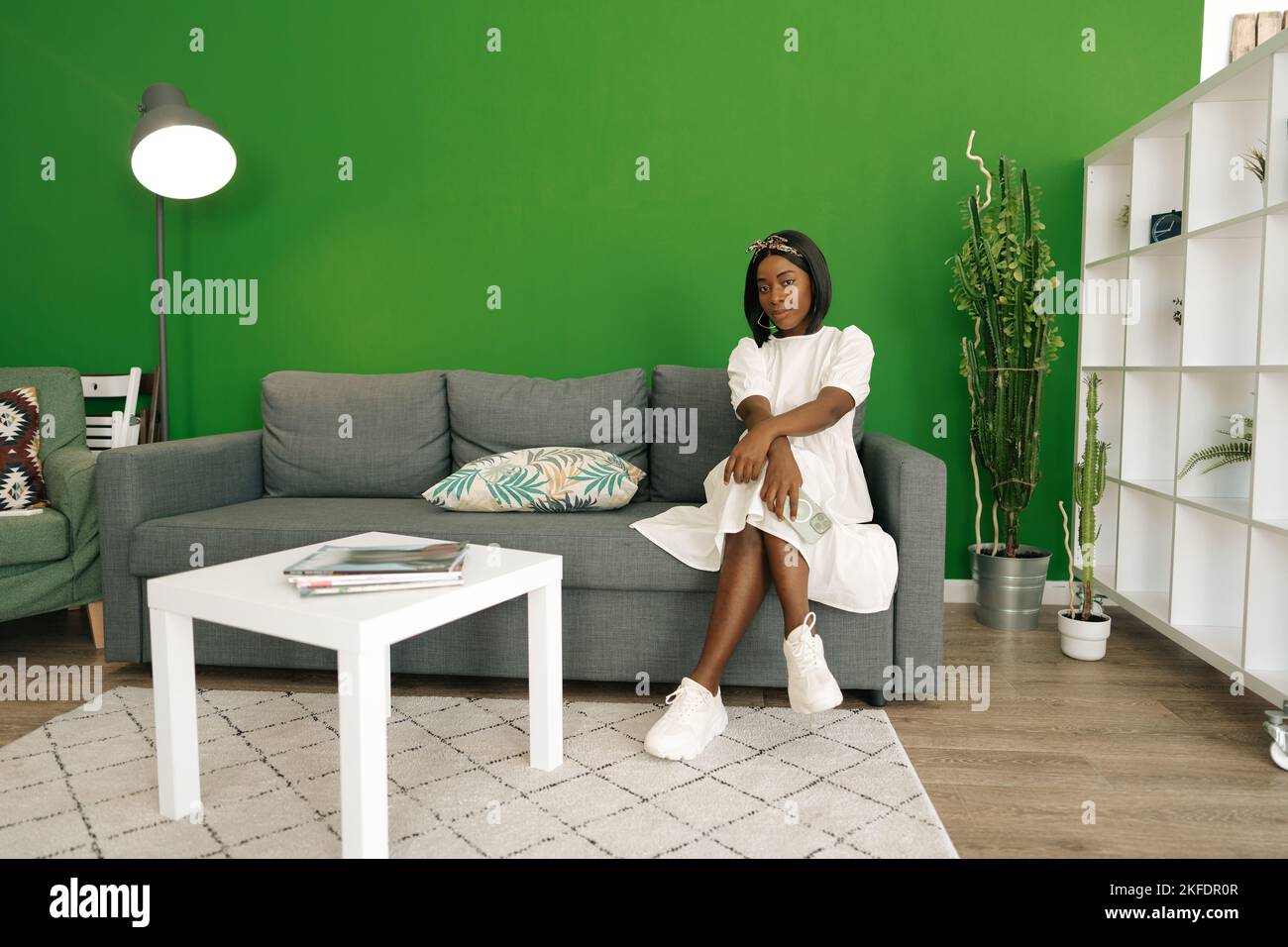 Young african woman sitting on couch at home and using smartphone Stock ...