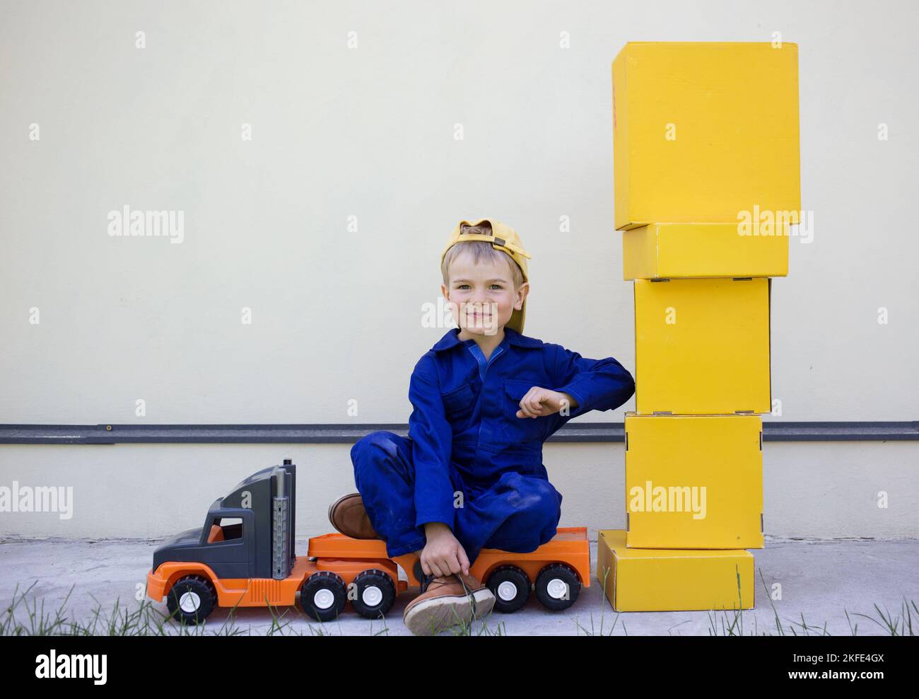 cute smiling 6 year old boy in blue uniform is sitting on big toy truck ...