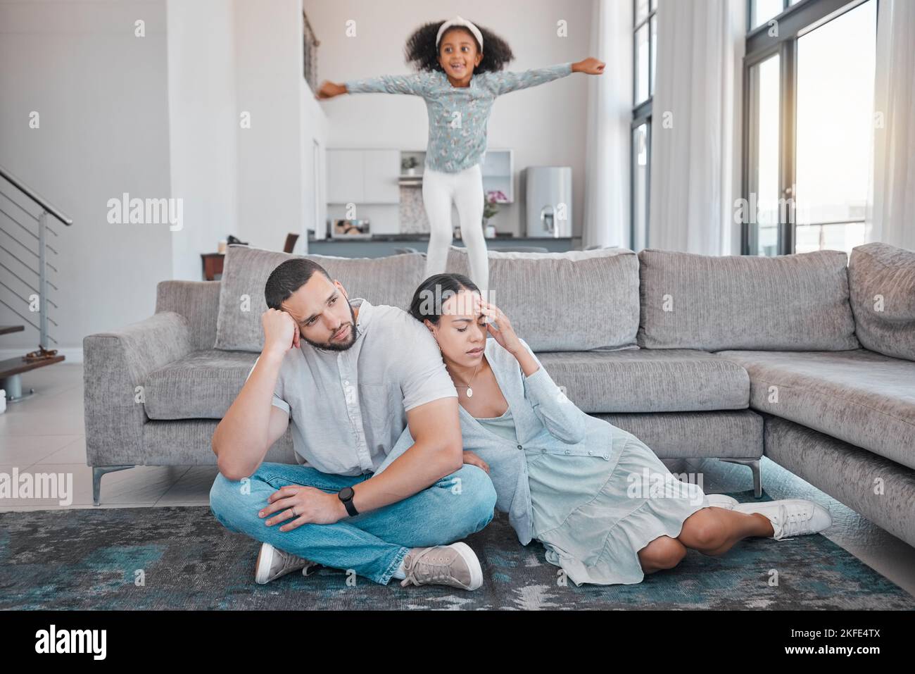 Tired, parents and child jump on sofa with exhausted mother and father sitting on floor in ...