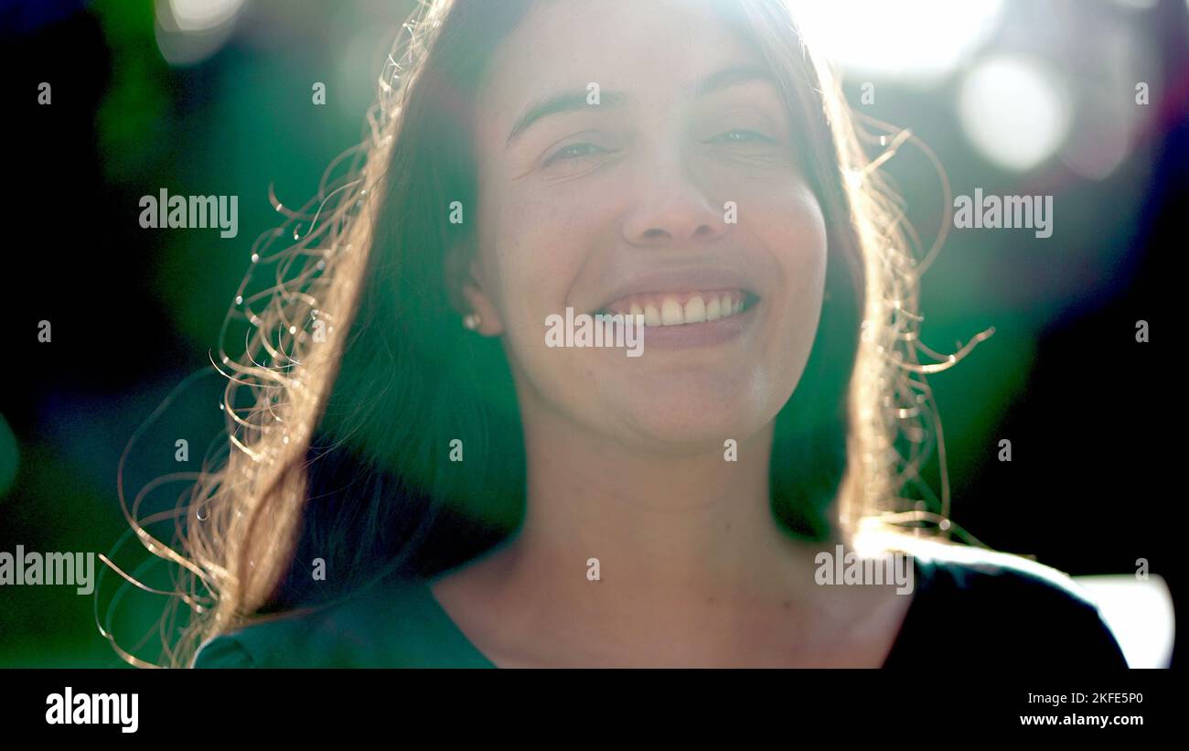 Woman in 30s smiling at camera standing outdoors with lens flare ...