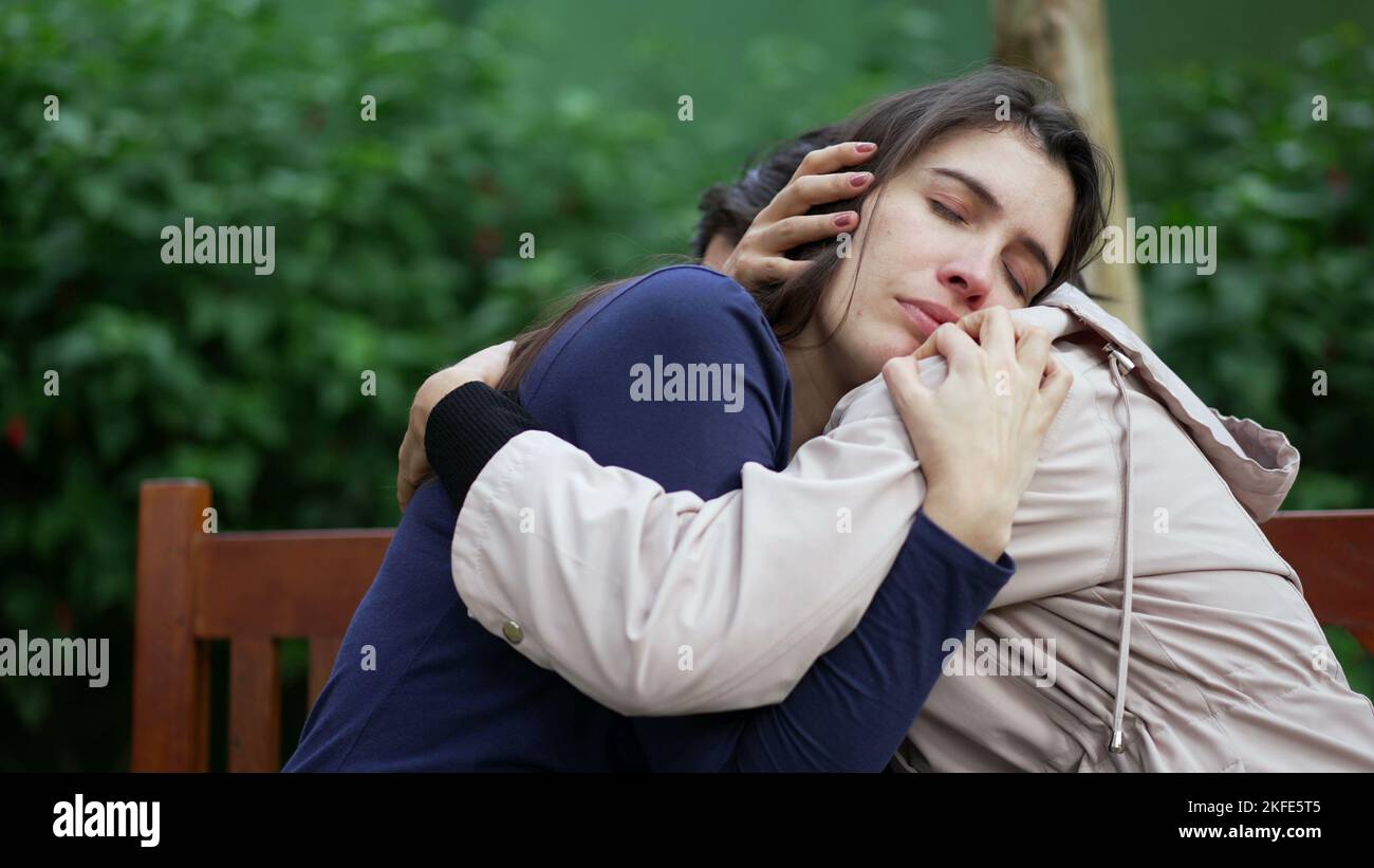 Supportive friend consoling suffering girl at park bench. Depressed ...