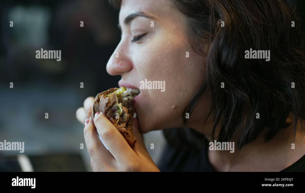A hispanic woman taking a bite of burger. A Latina American girl eating ...