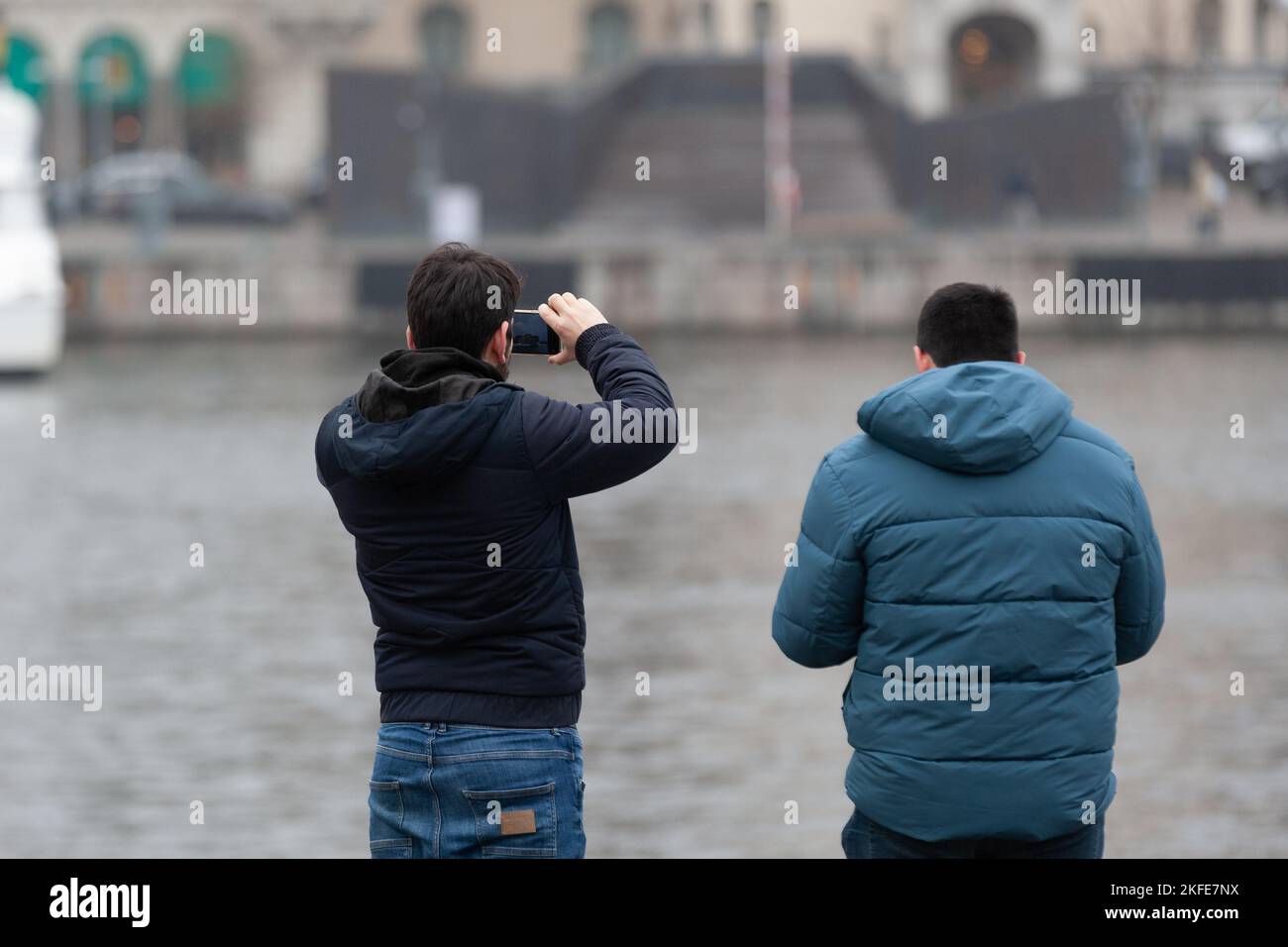 Two male tourists take pictures of the river view on the blurred ...