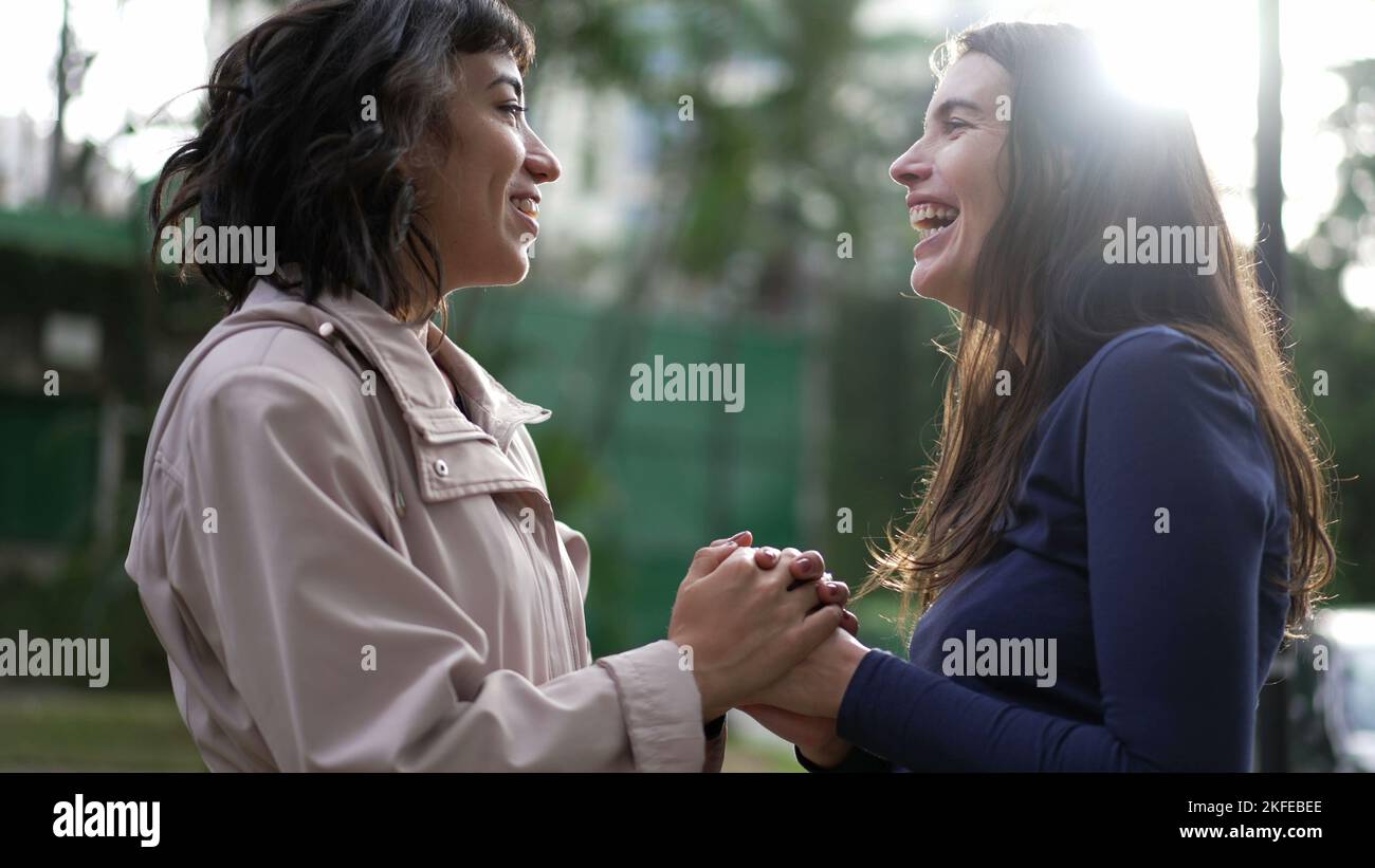 Happy female friends laughing and smiling standing outside in sunlight ...