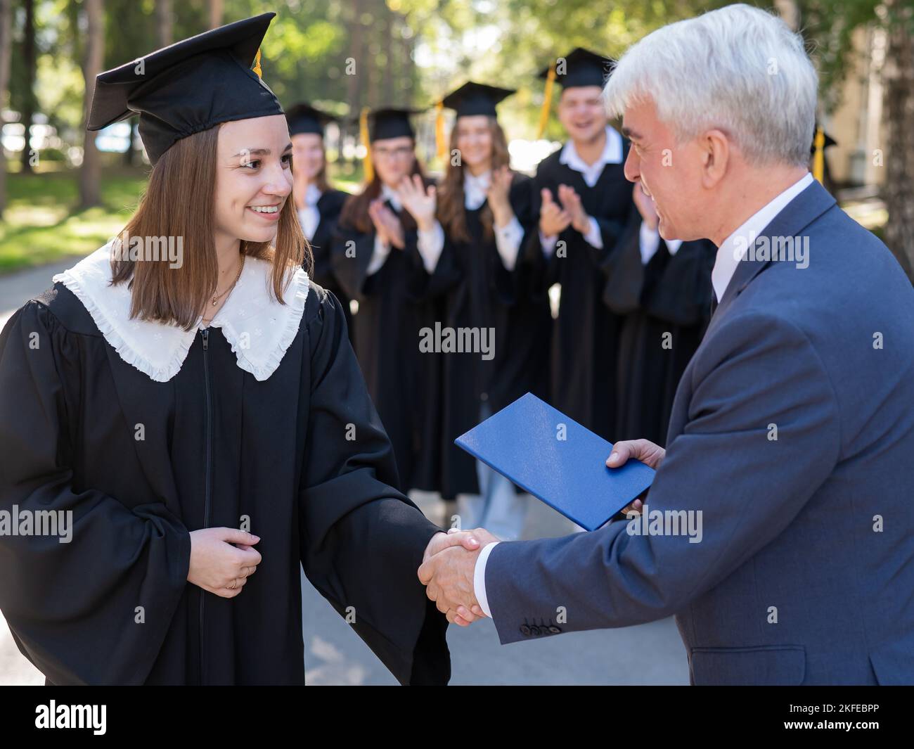 The teacher shakes hands with the student and presents the diploma ...