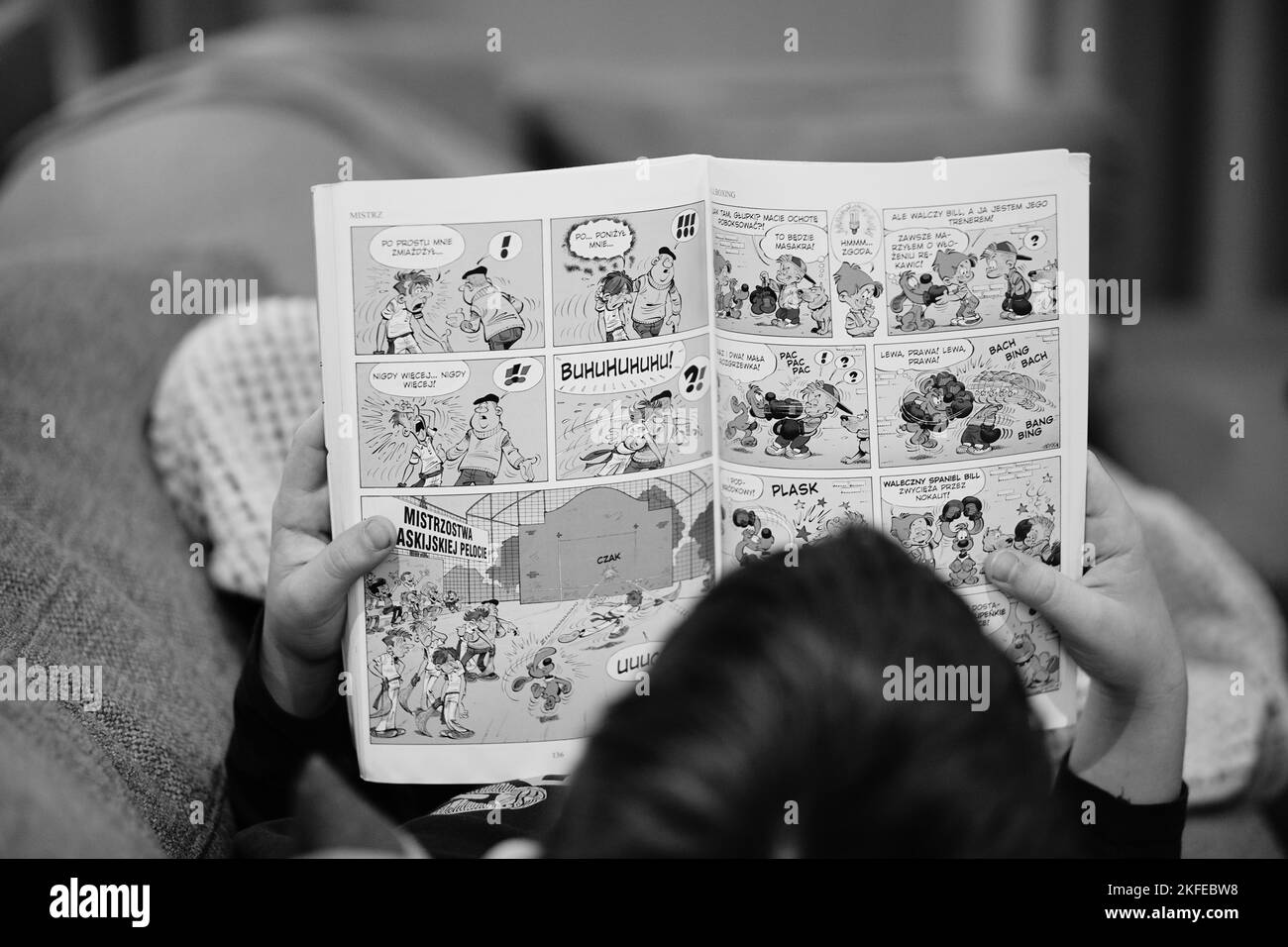 A child reading a Polish Ptys I Bill comic book on a sofa in a living ...
