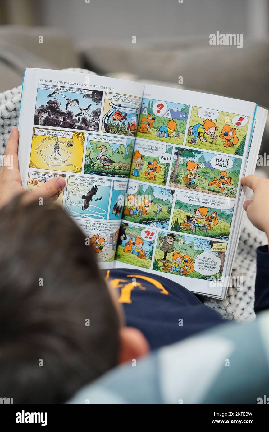 A child reading a Polish Ptys I Bill comic book on a sofa in a living ...